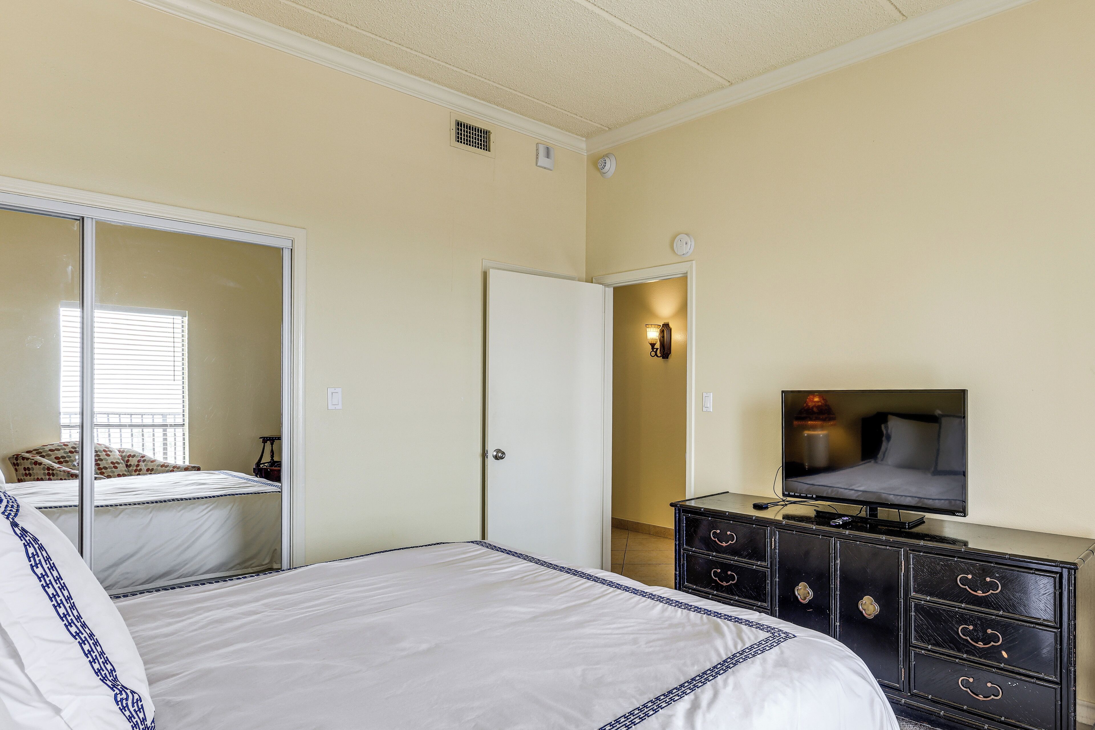 Quarto com cama, cômoda, televisão e porta que dá para outro espaço.