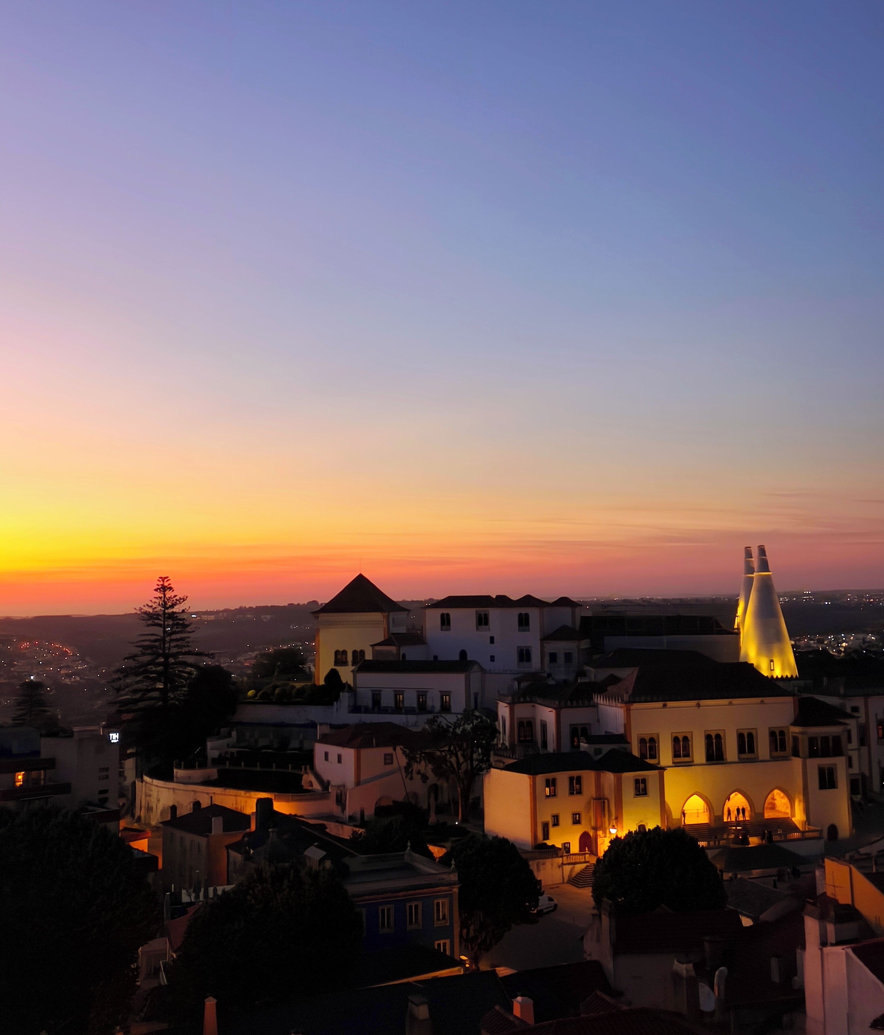 Uma cidade ao entardecer, com edifícios e uma torre imponente.
