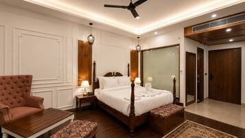 Quarto de hotel com cama, uma cadeira, mesa, banco, ventilador de teto e um espelho grande.
