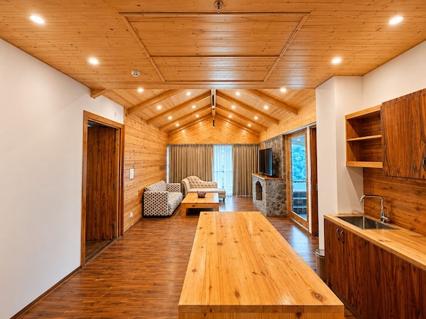 Um quarto amplo com teto de madeira, uma mesa de jantar comprida, lareira de pedra e televisão.