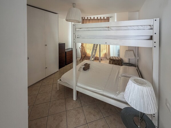 Uma cama beliche com cabeceira branca, luminária de cabeceira e uma pequena mesa com abajur.