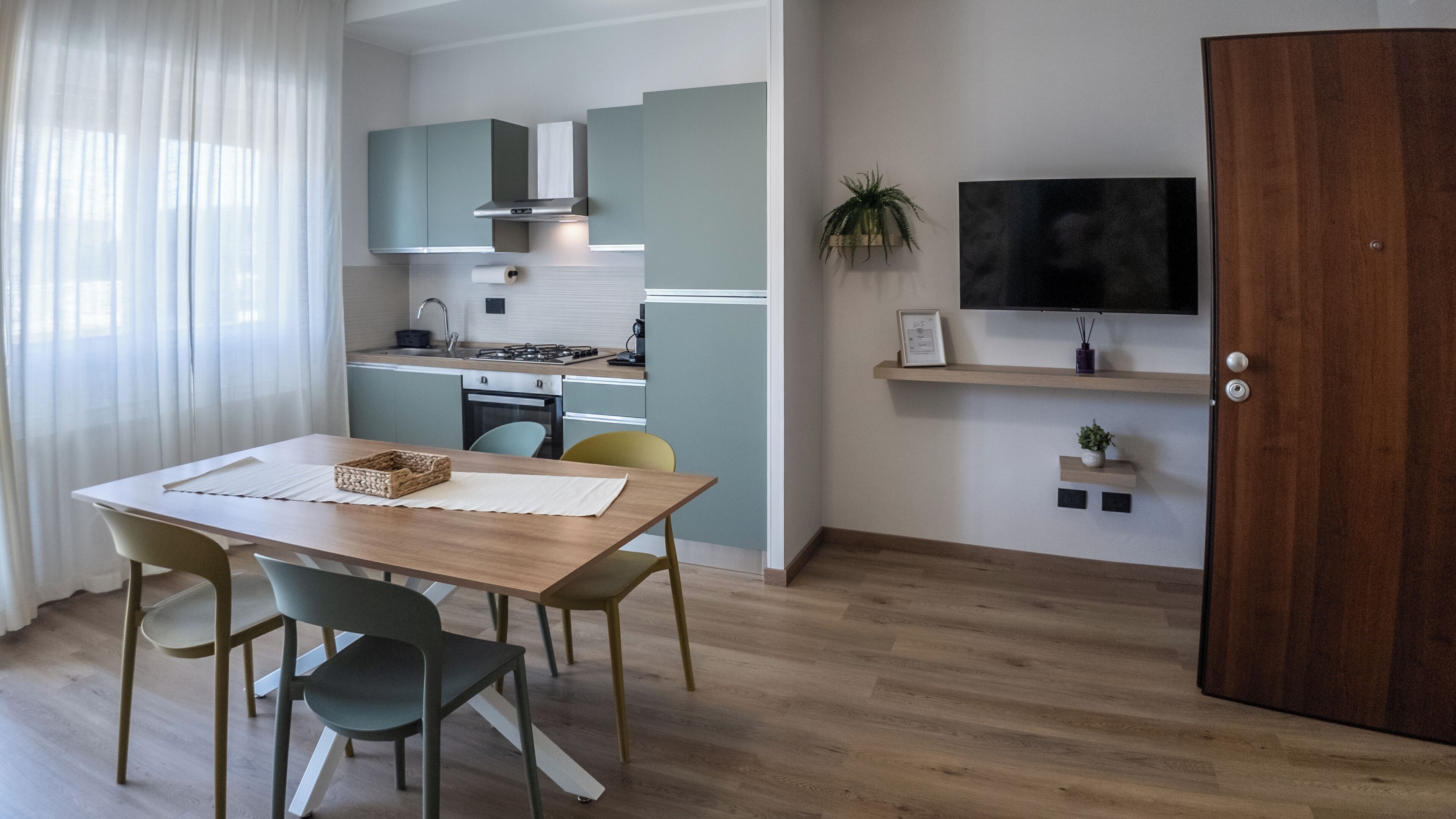 Uma cozinha moderna com área de jantar, televisão presa na parede e porta de madeira.
