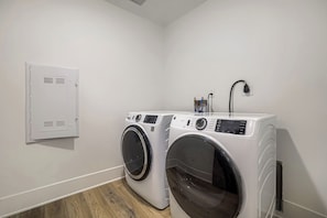 Uma lavanderia com duas máquinas de lavar de abertura frontal, um medidor de utilidades e um aquecedor de água.