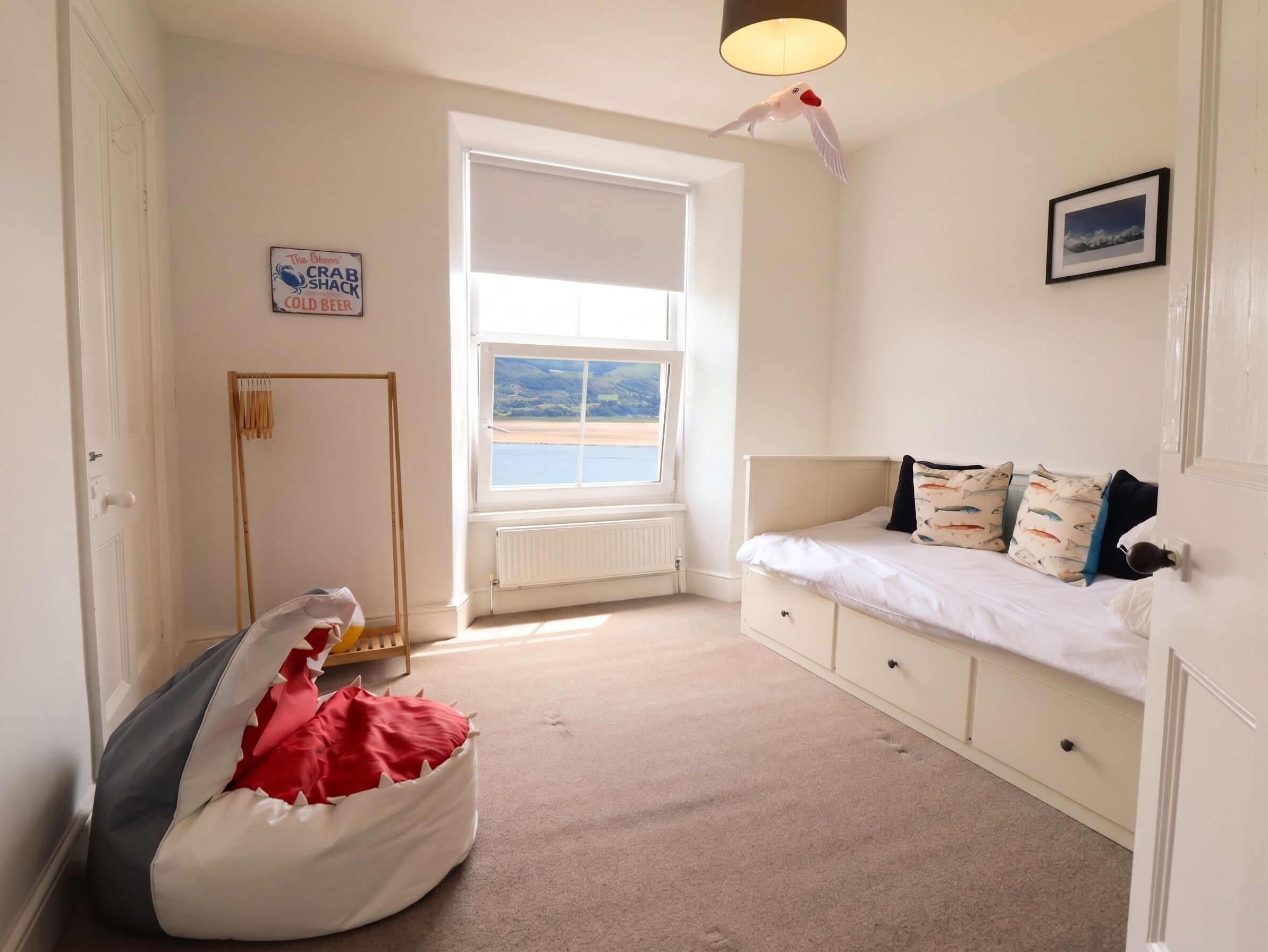 Quarto com cama, um bean bag, radiador, janela com vista e um aviso na parede.