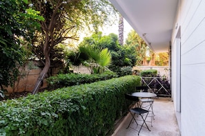 Um pátio com mesa e cadeiras, cercado por vegetação exuberante e uma árvore.