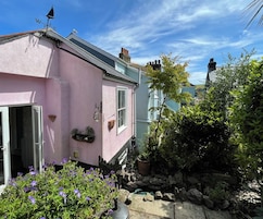 Uma casa rosa com jardim, um muro de pedra e um girassol.
