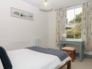 Quarto com cama, mesa de cabeceira com abajur, cadeira e janela com cortinas.