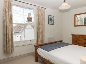 Um quarto com uma cama, uma cômoda de madeira, uma janela com cortinas, um radiador e um quadro na parede.