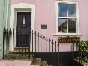Um edifício rosa com porta preta, janela com moldura branca e uma placa com a inscrição 'TILLER COTTAGE'.