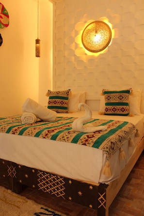 Cama com colcha estampada, duas almofadas e uma almofada em forma de cisne, além de luminária fixa na parede.