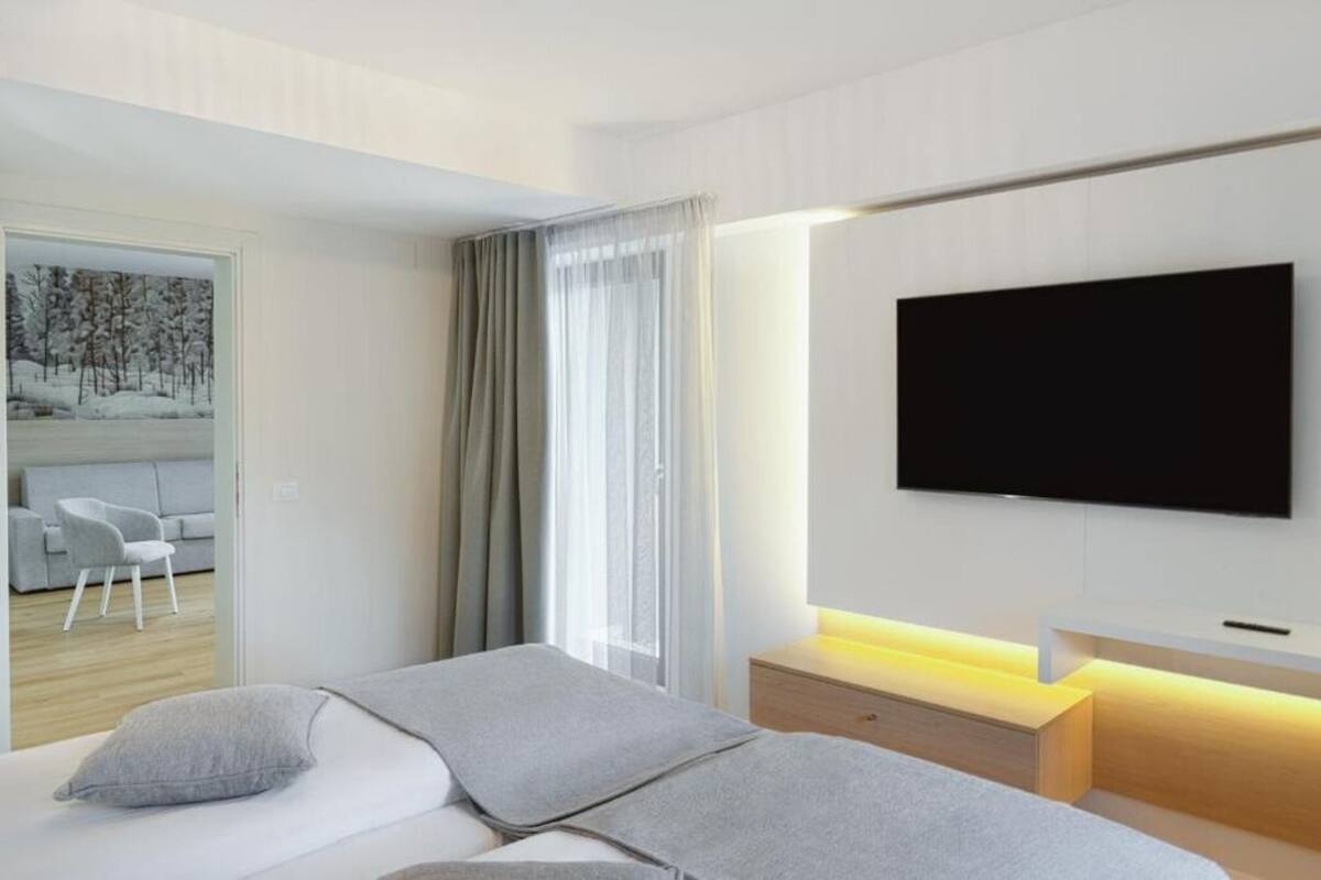 Quarto de hotel moderno com uma cama, uma televisão na parede e vista para uma paisagem nevada pela janela.