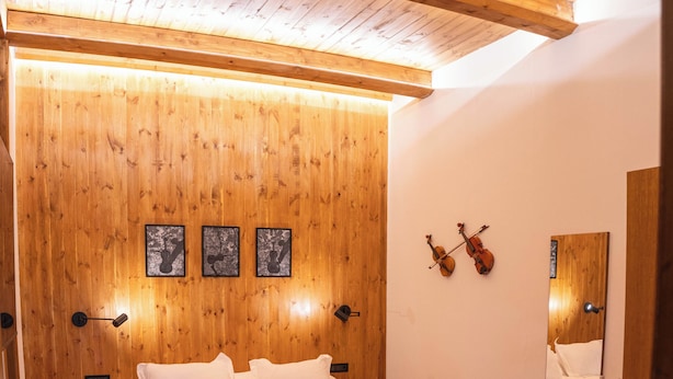 Quarto com painéis de madeira, cama, mesas de cabeceira, espelho e arte de um violino pendurado na parede.