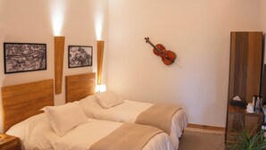 Quarto com duas camas, teto de madeira, luminárias fixadas na parede e uma decoração com um violino.
