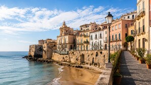 Uma cidade costeira com edifícios históricos, um muro de pedra e um calçadão pavimentado à beira-mar.