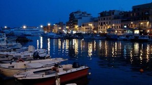Um porto ao entardecer com barcos atracados, edifícios iluminados e água calma refletindo as luzes.