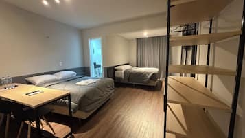 Quarto de hotel com cama, escrivaninha e cadeira. Há uma janela com cortinas e uma porta que dá para outro quarto.