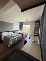 Quarto de hotel com duas camas, uma mesinha, varanda com vista e área de estar.