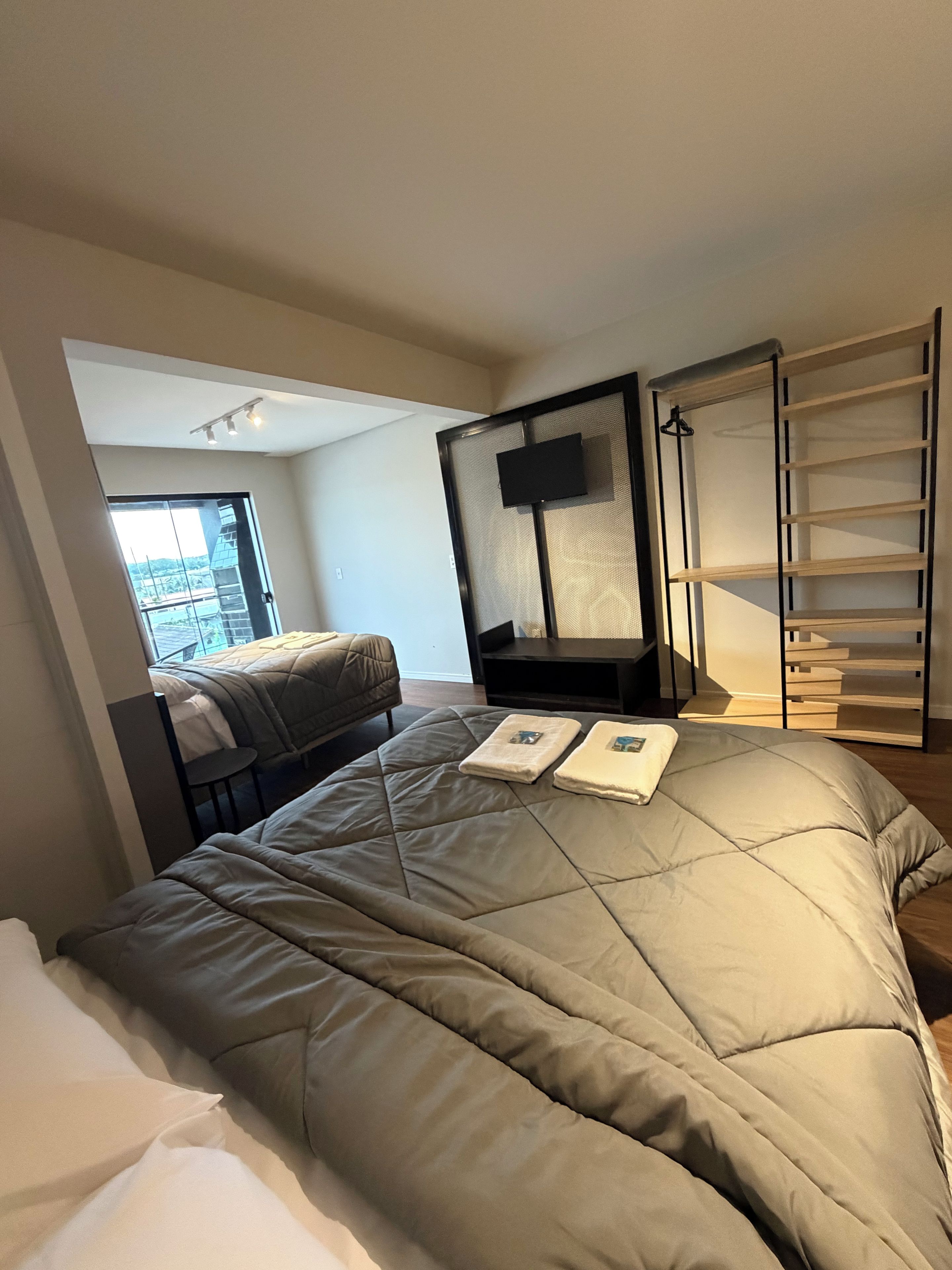 Quarto com cama, televisão em suporte, guarda-roupa e vista para o exterior.