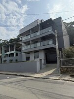 Um edifício residencial de vários andares com varandas, entrada com portão e um caminho de acesso pavimentado.