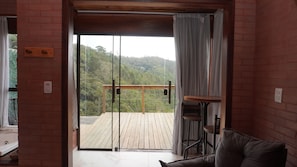 Quarto com porta de vidro deslizante que dá para um deck de madeira com vista para uma colina arborizada.