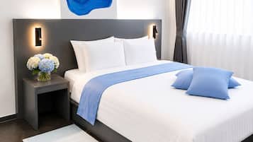 Quarto de hotel moderno com uma cama grande, uma mesa de cabeceira com um vaso de flores e uma pintura abstrata azul na parede.