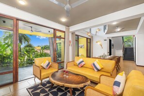 Uma sala de estar moderna com um sofá amarelo, uma mesa de centro redonda de madeira e uma área de jantar com tapete preto e branco.