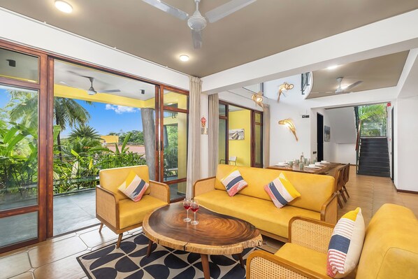 Uma sala de estar moderna com um sofá amarelo, uma mesa de centro redonda de madeira e uma área de jantar com tapete preto e branco.