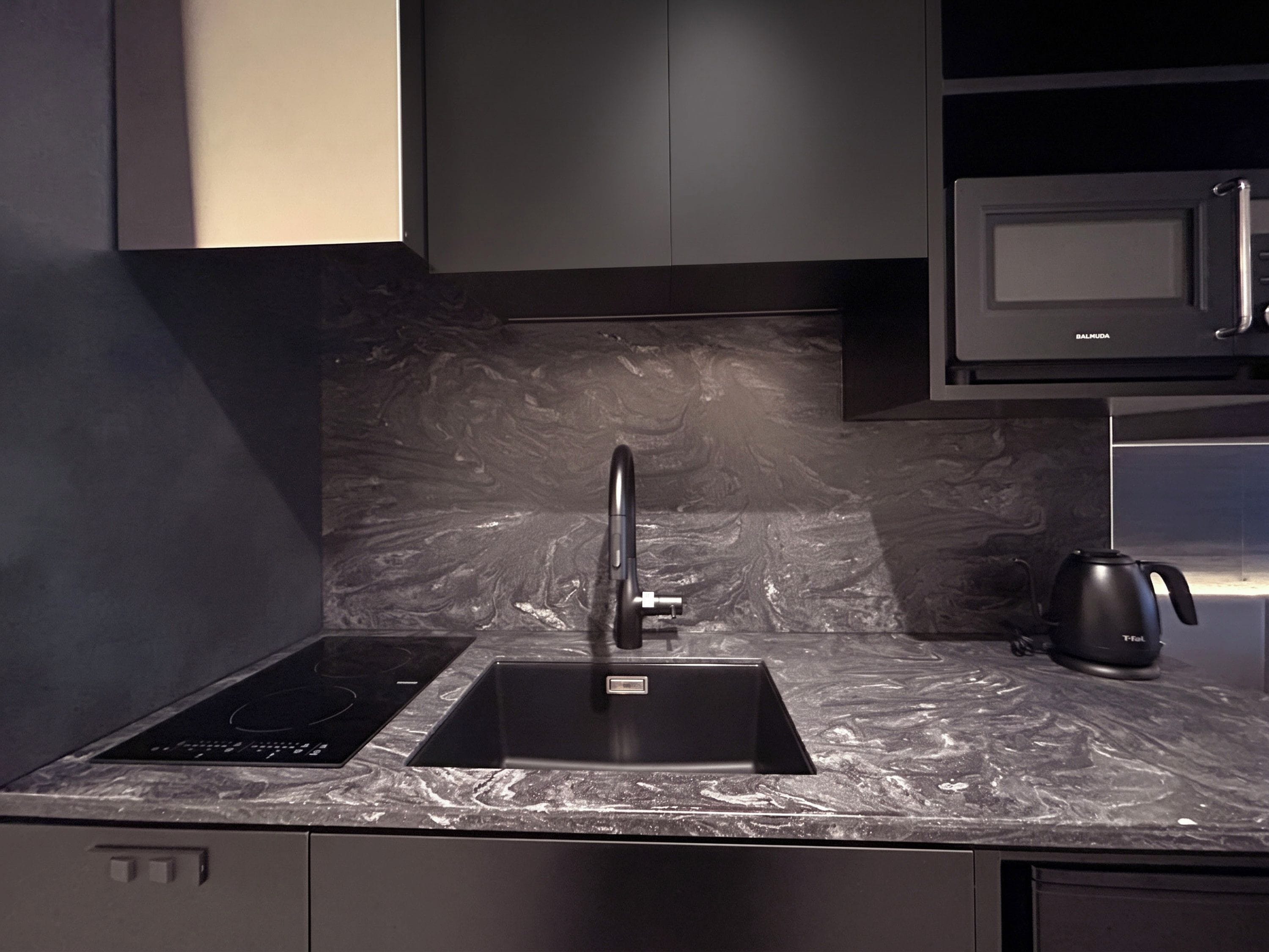 Cozinha moderna com bancada preta, pia de aço inoxidável, micro-ondas embutido e chaleira preta.