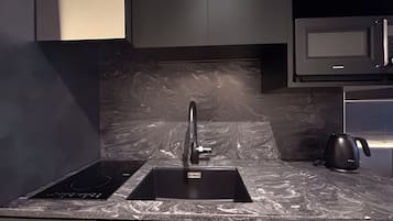 Cozinha moderna com bancada preta, pia de aço inoxidável, micro-ondas embutido e chaleira preta.
