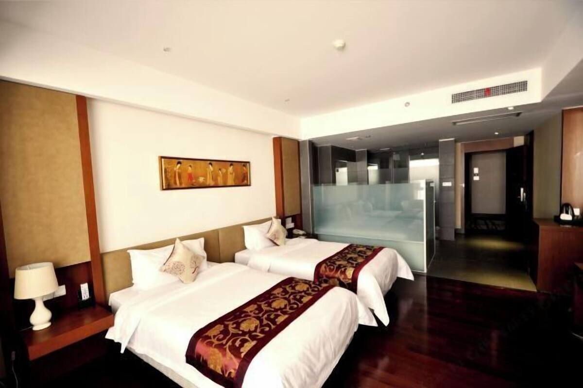 Quarto de hotel com duas camas, uma mesa de cabeceira, um abajur, um quadro na parede e um painel de vidro.
