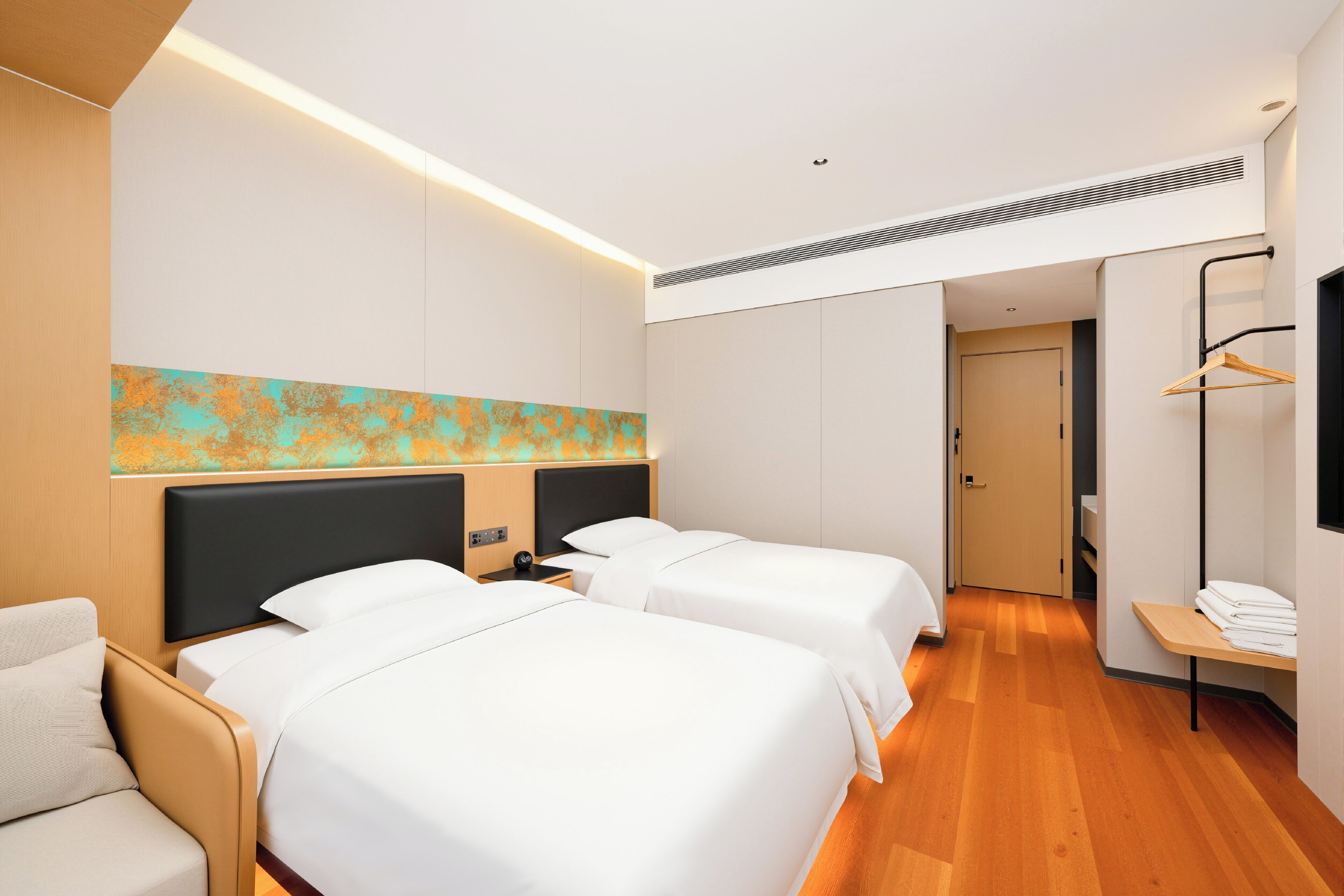 Quarto de hotel com duas camas, um sofá, uma televisão e um banheiro visível através de uma porta aberta.