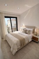 Quarto com uma cama grande, mesa de cabeceira, abajur e vista pela porta de correr.