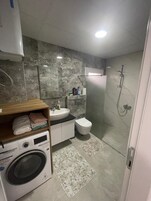 Casa de banho compacta com máquina de lavar embutida, lavatório e chuveiro.