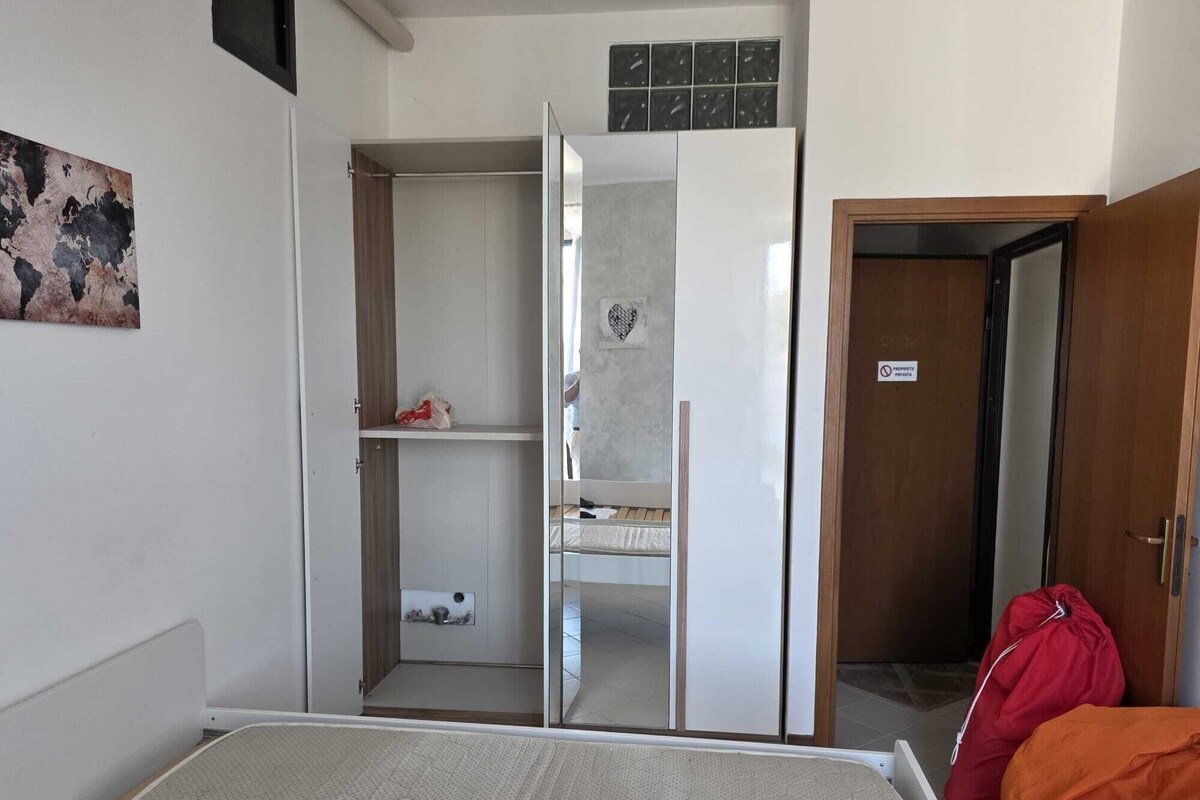 Quarto com uma cama, um guarda-roupa, um espelho e uma porta.