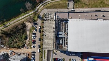 Vista aérea de um estacionamento com vários carros, um edifício de telhado plano e um corpo d'água ao fundo.