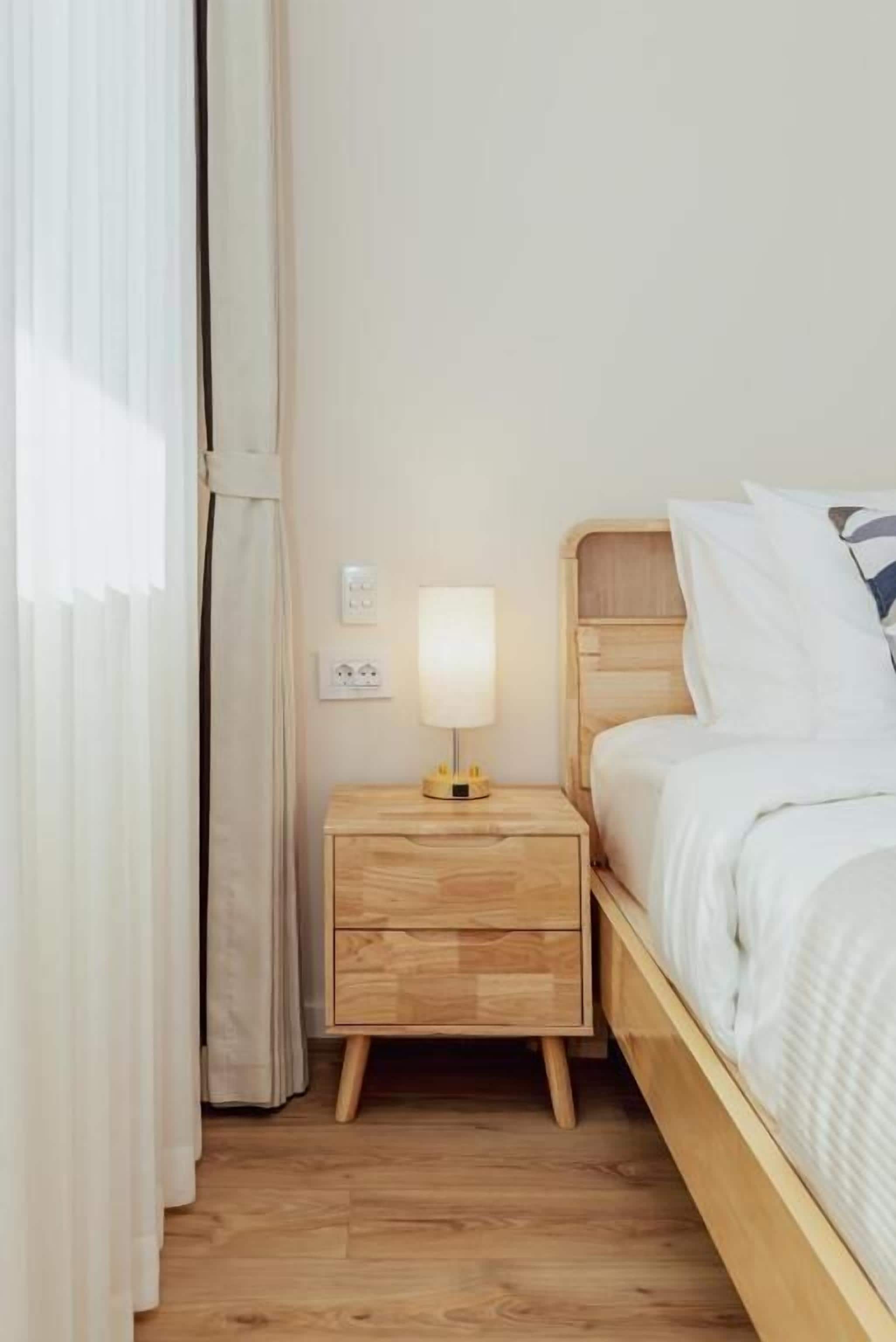 Quarto de hotel com cama de madeira, mesa de cabeceira com abajur e tomada na parede.