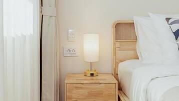 Quarto de hotel com cama de madeira, mesa de cabeceira com abajur e tomada na parede.