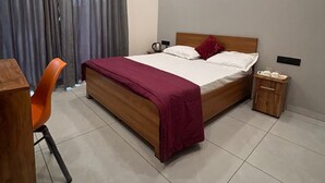Quarto com cama, escrivaninha, cadeira, mesa de cabeceira e ventoinha no teto.