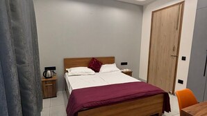 Quarto com cama, mesa de cabeceira, escrivaninha, cadeira, ventoinha no teto e guarda-roupa.