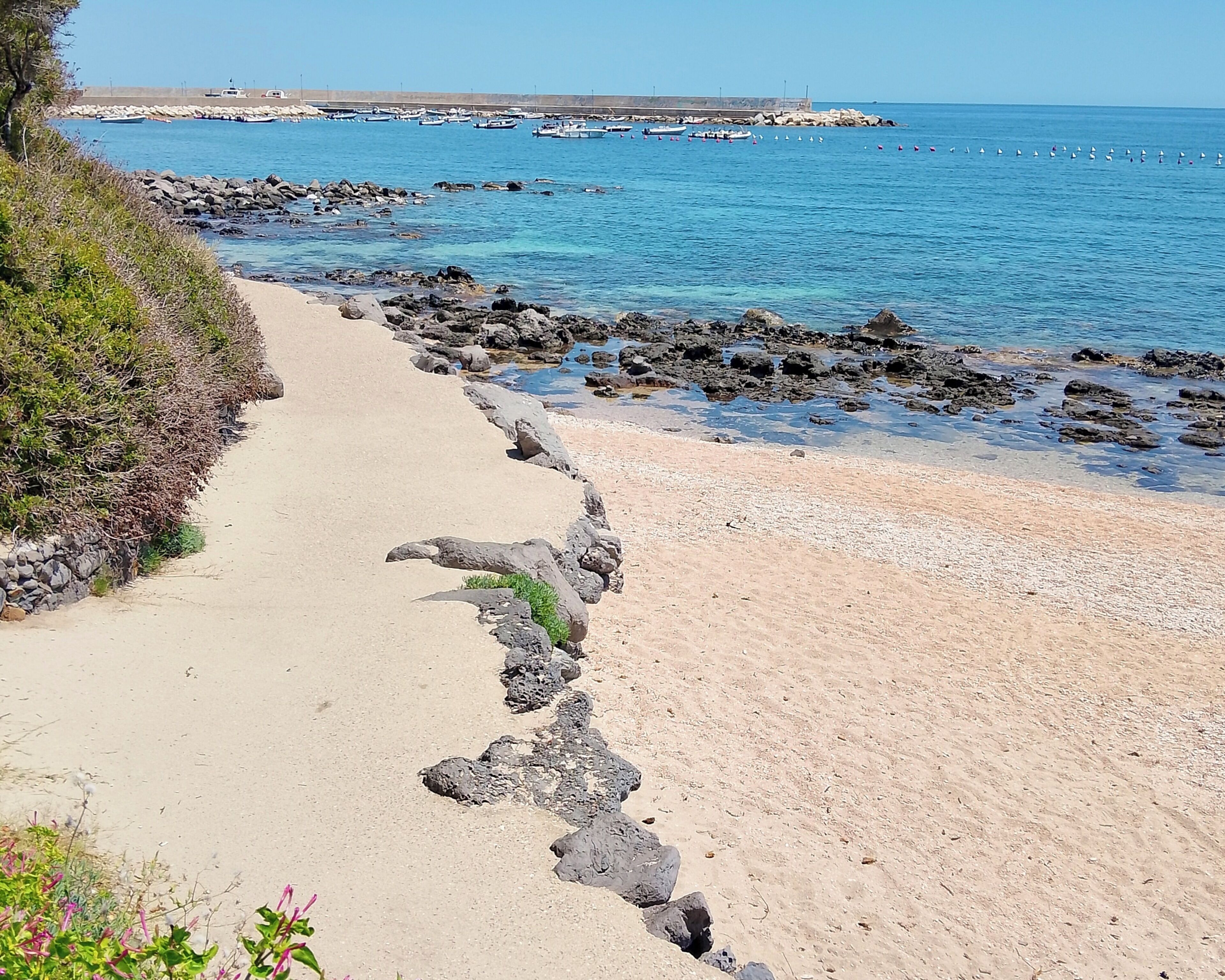 Um caminho costeiro com uma praia arenosa e afloramentos rochosos.
