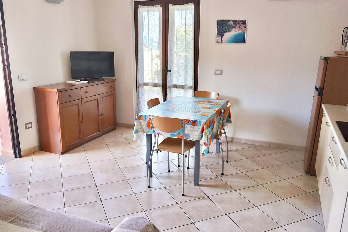 Uma área de refeições com mesa, cadeiras, uma televisão num armário e um quadro na parede.