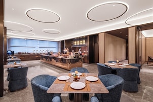 Um restaurante moderno com área de bar, mesas redondas e cadeiras azuis.
