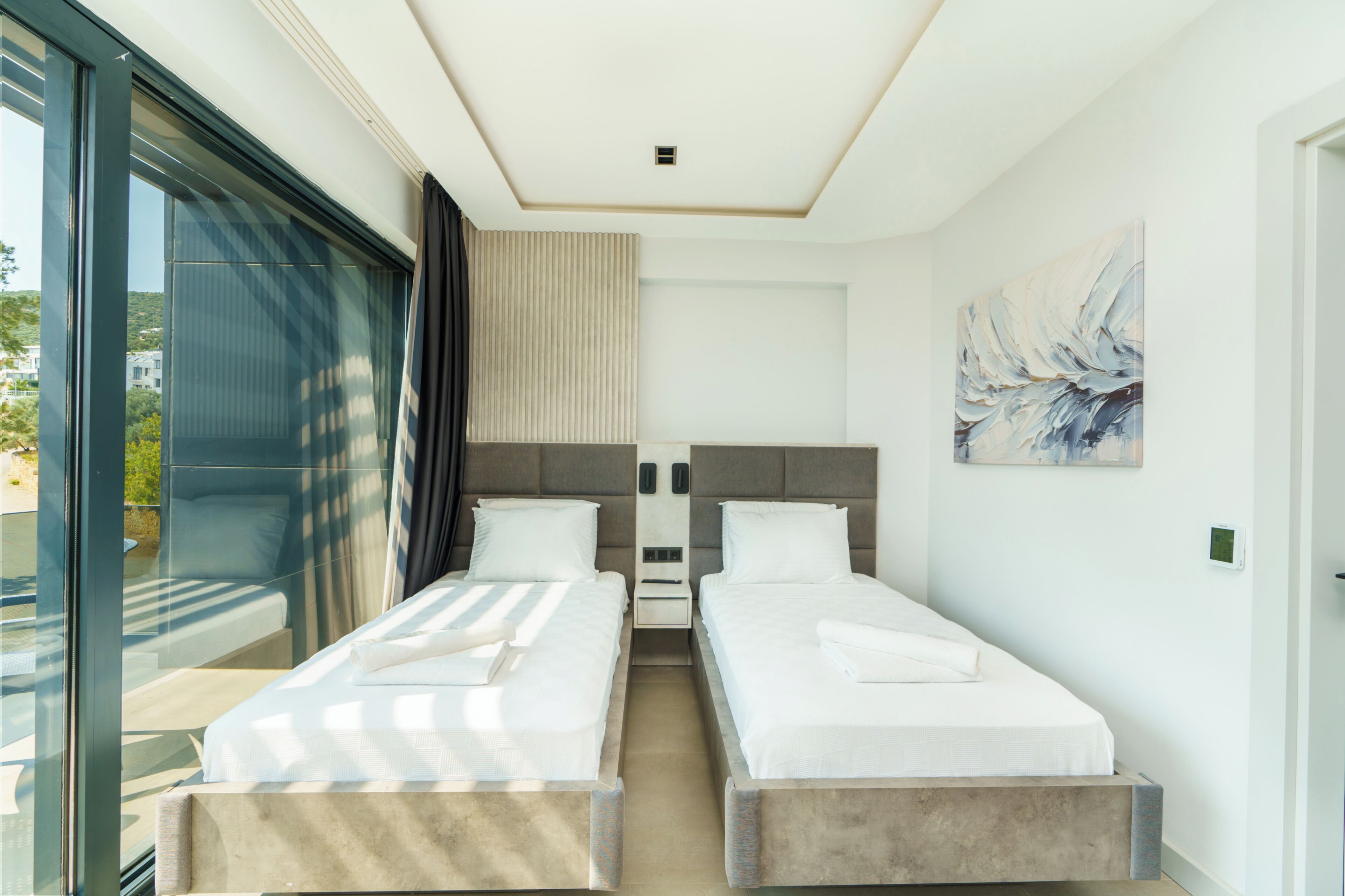 Quarto de hotel moderno com duas camas, uma janela grande e um quadro na parede.