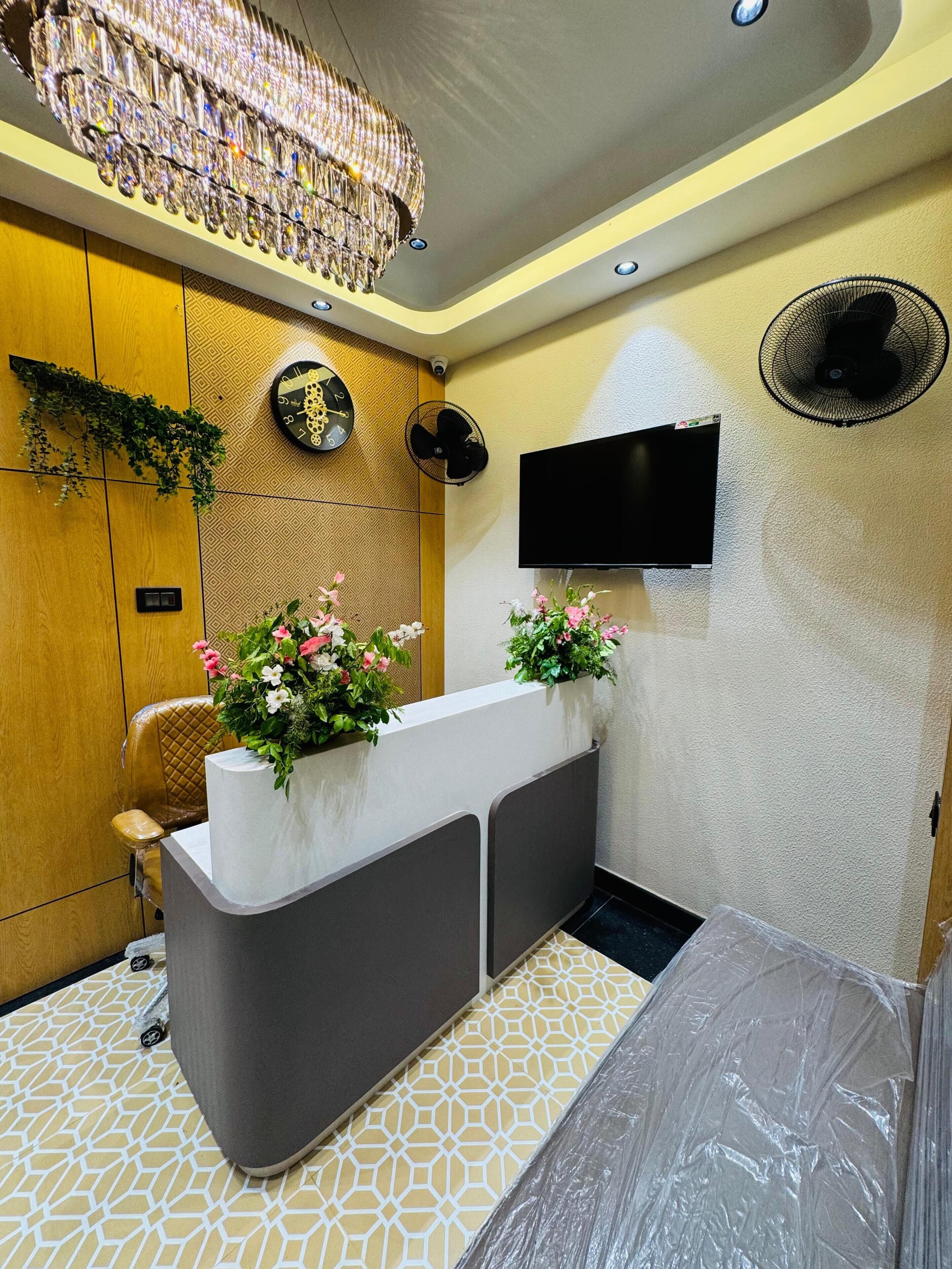 Uma área de recepção com design moderno, incluindo um balcão de atendimento, um relógio, uma televisão e um lustre decorativo.