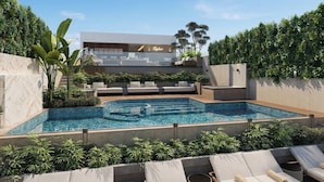 Uma área de piscina moderna ao ar livre, com espreguiçadeiras, um edifício de spa e vegetação exuberante.