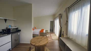 Quarto de hotel compacto com cozinha compacta, área de refeições, cama e uma janela grande com cortinas.