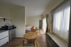Quarto de hotel compacto com cozinha compacta, área de refeições, cama e uma janela grande com cortinas.