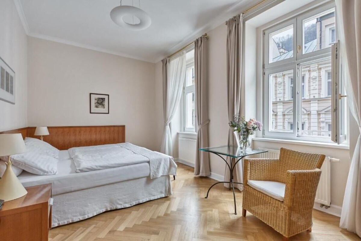 Quarto de hotel com cama, poltrona, mesa e janela com cortinas.