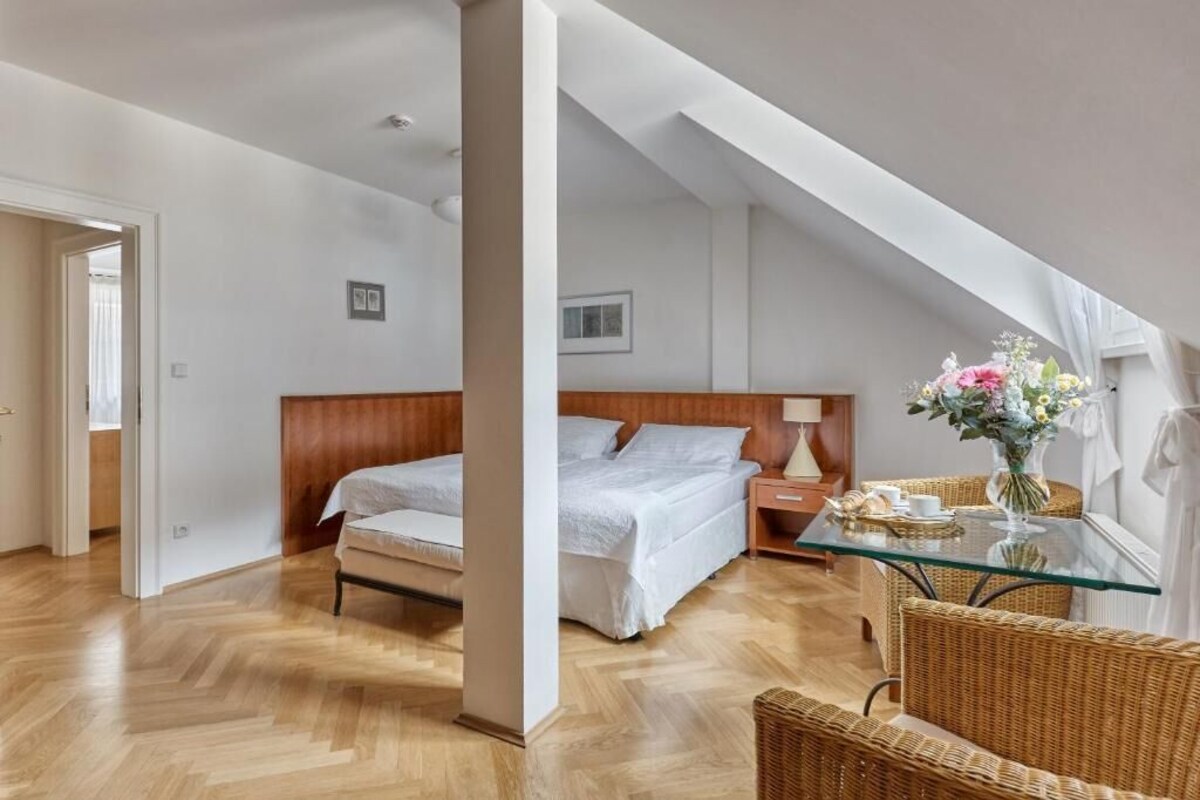 Quarto com cama de madeira, mesa de vidro com um vaso e uma cadeira de vime.
