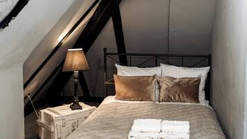 Um quarto com cama, almofadas, mesa de cabeceira, abajur e mala.